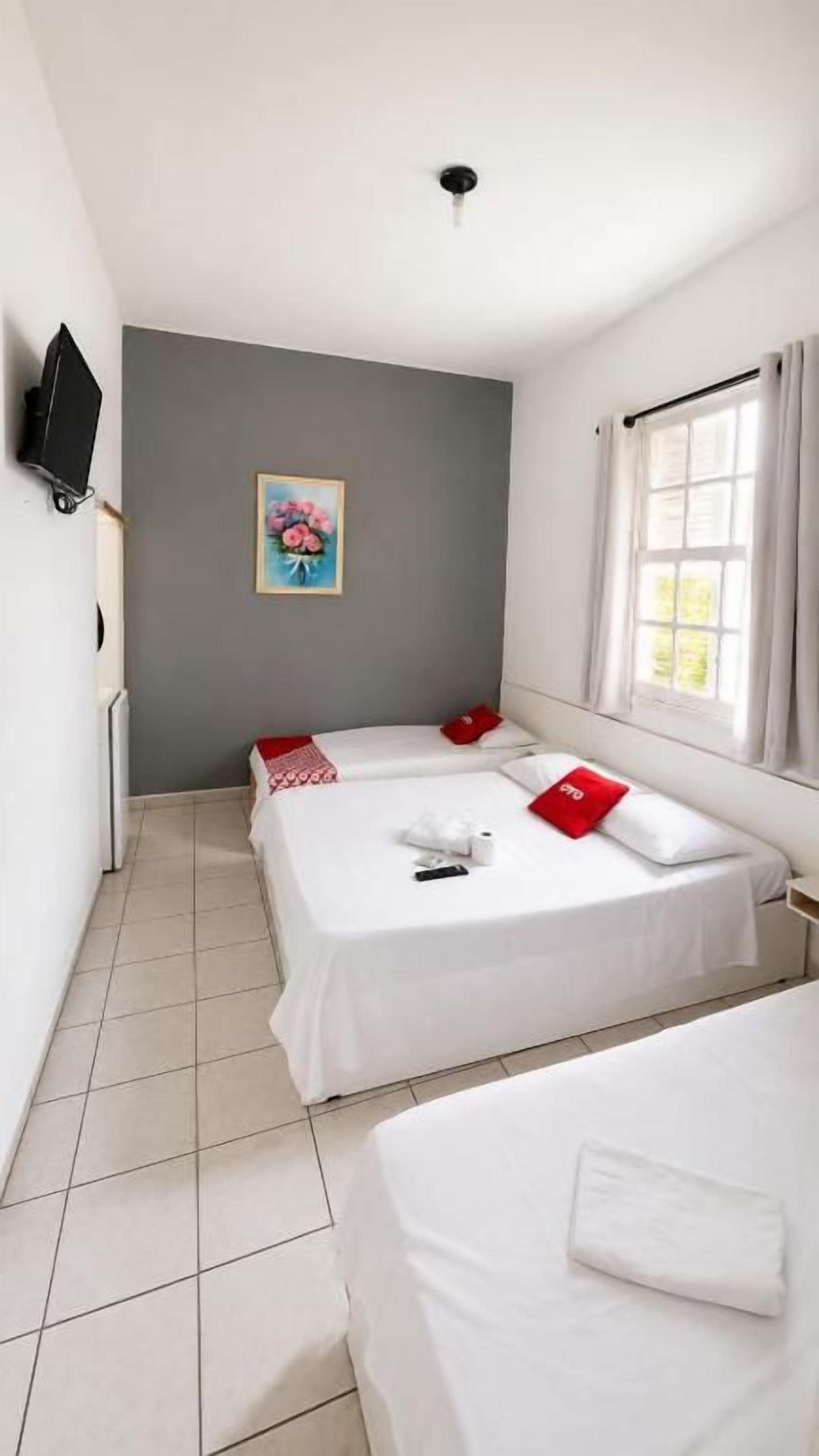 Quarto de hotel com duas camas, televisão de tela plana, um quadro e uma janela com cortinas.