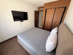 Quarto com cama, televisão na parede e guarda-roupa de madeira.