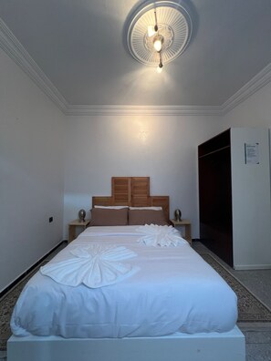Quarto de hotel com cama, cabeceira de madeira, luminária no teto e armário.