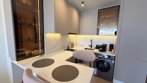 Cozinha compacta com forno embutido, máquina de lavar e cafeteira.