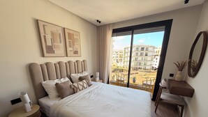 Quarto de hotel com uma cama grande, uma mesinha redonda, uma cadeira, um espelho e vista para a cidade pela janela.