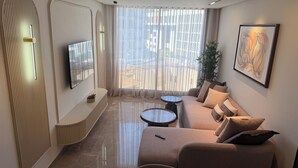 Uma sala de estar moderna com um sofá, uma mesa de centro, uma televisão e uma janela grande com cortinas.