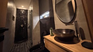 Uma casa de banho moderna com um espelho grande, uma sanita preta e zona de duche.