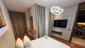 Quarto moderno com cama grande, televisão na parede, máquina de lavar embutida e um banco de madeira.