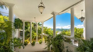 Uma área externa coberta com colunas, plantas em vasos e vista para a paisagem.