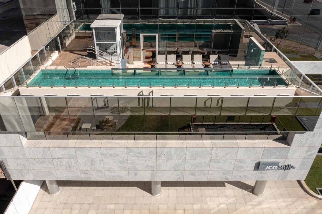 Piscina no terraço com cobertura de vidro, rodeada por um edifício moderno com fachada revestida de azulejos.