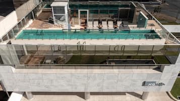 Piscina no terraço com cobertura de vidro, rodeada por um edifício moderno com fachada revestida de azulejos.