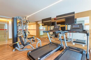 Academia com esteiras, aparelhos de musculação e um painel digital.