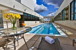 Piscina com espreguiçadeiras e mesa de vidro adornada com flores.