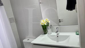 Um banheiro com pia branca, espelho e vaso sanitário. Há um buquê de flores sobre a pia.