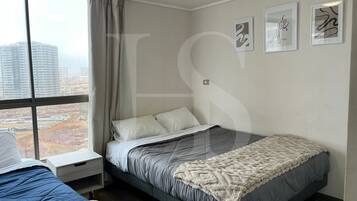 Quarto com cama, mesa de cabeceira, janela com cortinas e três quadros na parede.