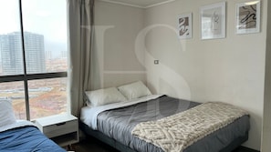 Quarto com cama, mesa de cabeceira, janela com cortinas e três quadros na parede.