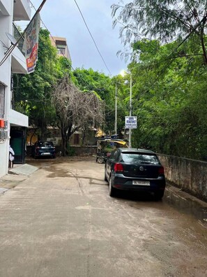 Uma rua estreita com carros estacionados, uma placa e vegetação.