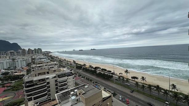Paisagem costeira com praia, edifícios altos e uma estrada com veículos.