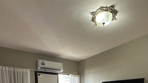 Quarto de hotel com cama, escrivaninha, televisão de tela plana na parede, ar condicionado sobre a janela e vista para o exterior pela janela.