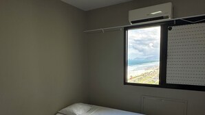 Quarto com duas camas, janela com vista para a praia e ar condicionado.