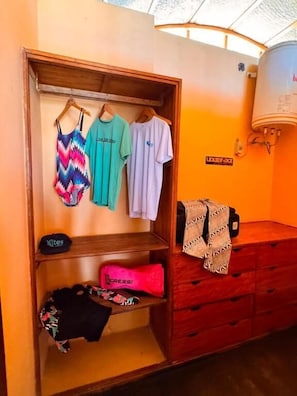 Quarto com guarda-roupa de madeira, prateleira com roupas dobradas e aquecedor fixado na parede.