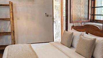 Quarto com cama, cabeceira de madeira, luminária de fibra e porta com detalhes decorativos.