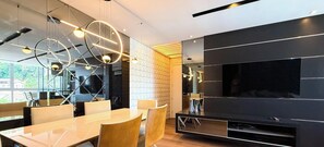 Uma área de refeições moderna com uma TV grande, móveis contemporâneos e uma luminária de teto diferenciada.