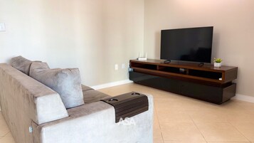 Uma sala de estar moderna com um sofá, uma televisão em um suporte de madeira e uma pequena planta.