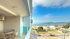 Varanda com mesa e cadeiras, com vista para uma vila costeira e montanhas.
