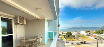 Varanda com mesa e cadeiras, com vista para uma vila costeira e montanhas.