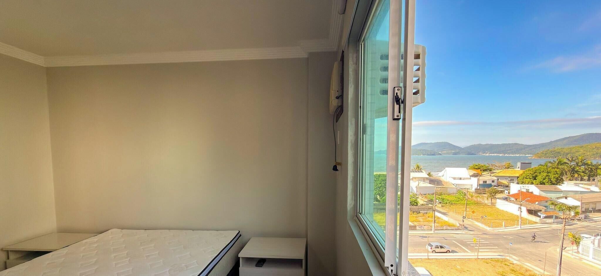 Quarto com uma janela grande, uma cama e vista para uma vila costeira.