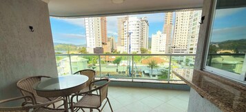 Varanda com mesa de vidro e cadeiras de vime, com vista para um horizonte urbano repleto de arranha-céus.