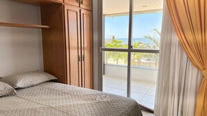 Quarto com cama, guarda-roupa e varanda com vista para o mar.