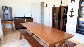 Cozinha compacta com geladeira embutida, mesa de madeira com bancos e armário com portas de vidro.