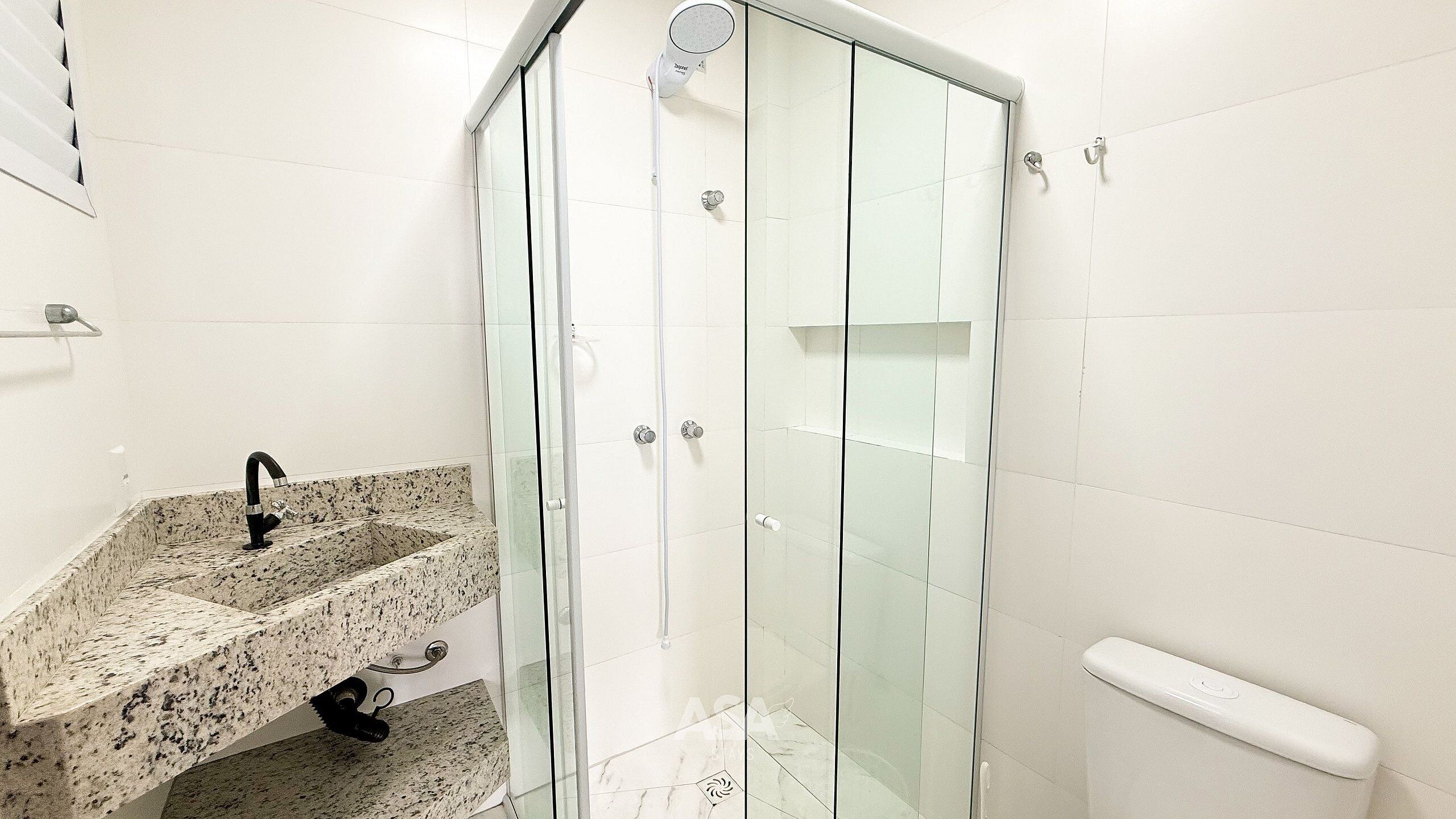 Um banheiro moderno com box de vidro, pia com bancada de granito e vaso sanitário branco.
