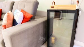 Sala de estar com sofá cinza, almofadas coloridas e um minibar com uma garrafa.
