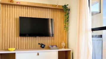 Uma sala de estar moderna com uma televisão de tela plana presa a uma parede de madeira, uma pequena planta e um recipiente de vidro sobre uma mesa de console branca.