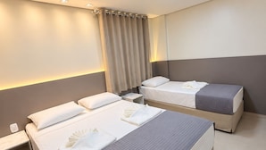 Quarto de hotel com duas camas, uma mesa de cabeceira e uma cortina.