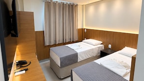 Quarto de hotel com duas camas, uma escrivaninha, televisão e banheiro com cortina de chuveiro.