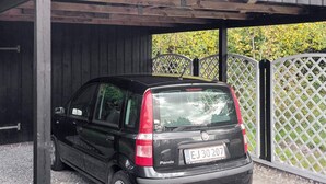Um carro preto estacionado sob uma marquise de madeira com um portão de treliça ao fundo.
