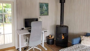 Quarto com escrivaninha, cadeira, cama, lareira a lenha preta e janela com vista para o verde.
