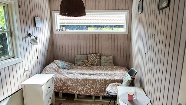 Quarto com cama, escrivaninha, cadeira, janela e luminária pendente.