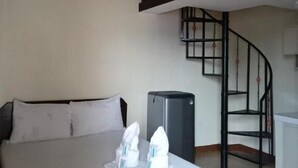 Quarto de hotel com cama, uma pequena escrivaninha, um cesto de lixo e uma escada em espiral.