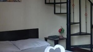Quarto de hotel com uma cama, arranjo de toalhas em formato de coração, um quadro na parede e uma escada.
