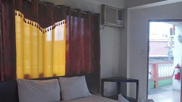 Quarto de hotel com cama, cortinas, mesa de cabeceira e vista para o exterior.