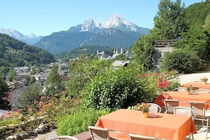 Restaurante com mesas ao ar livre, com vista para uma paisagem montanhosa.