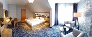 Quarto de hotel com cama, escrivaninha, poltrona, sofá e luminária.