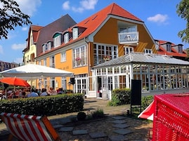 Hotel com fachada amarela, telhado vermelho e área de estar externa coberta com guarda-sóis.