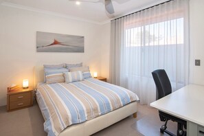 Quarto de hotel com cama, mesas de cabeceira, escrivaninha e cadeira.