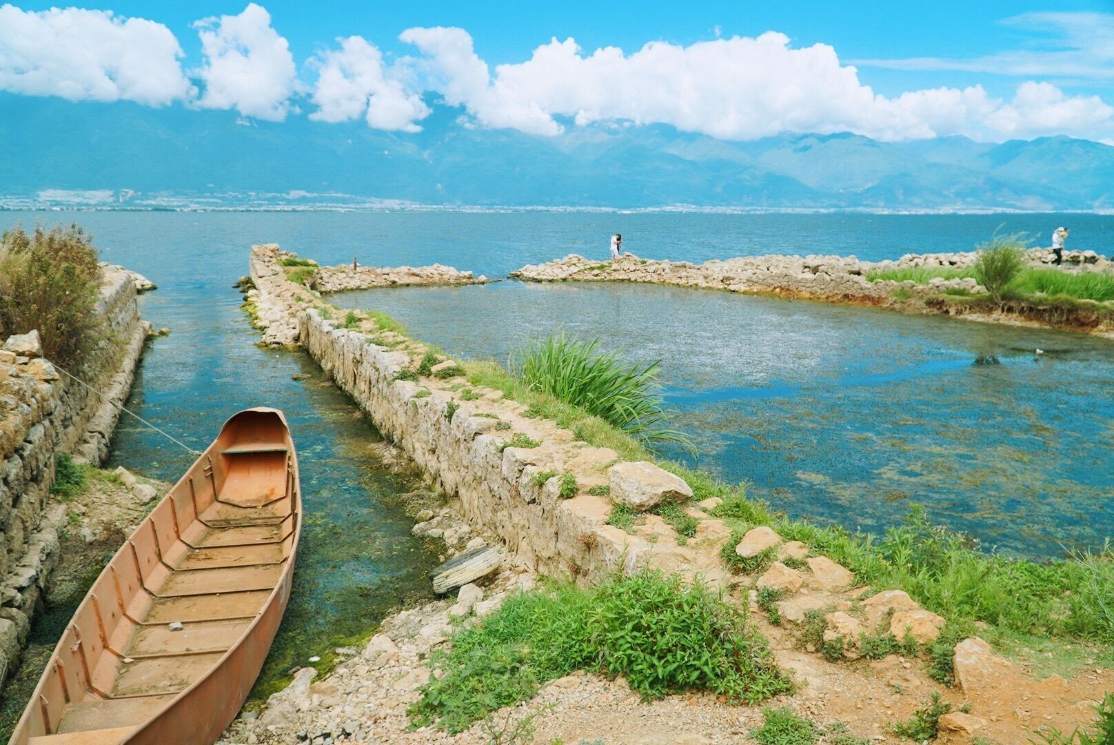 Um rio com um barco de madeira, margens rochosas e vista distante de montanhas.