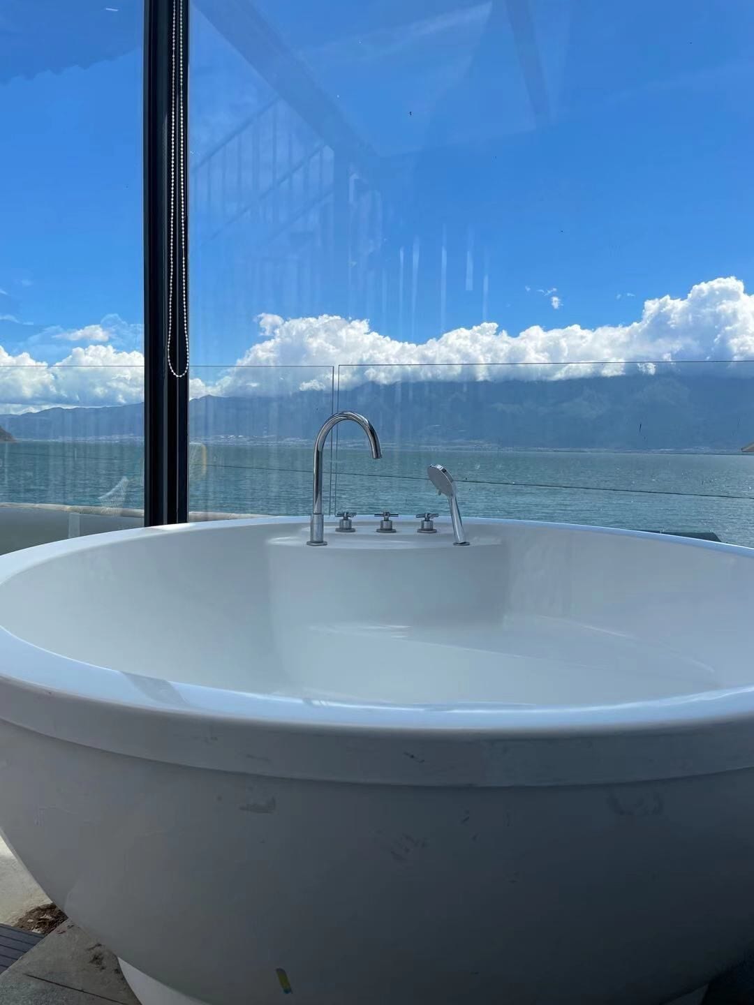 Uma banheira com vista para a água e montanhas pela janela.