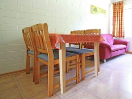 Uma sala de jantar com cadeiras de madeira e uma mesa, um sofá rosa e uma janela com cortinas.