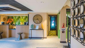 Uma área de recepção de hotel com balcão, um relógio de parede grande e uma parede decorativa com espelhos.