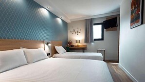 Quarto de hotel com duas camas, uma escrivaninha, televisão e janela.